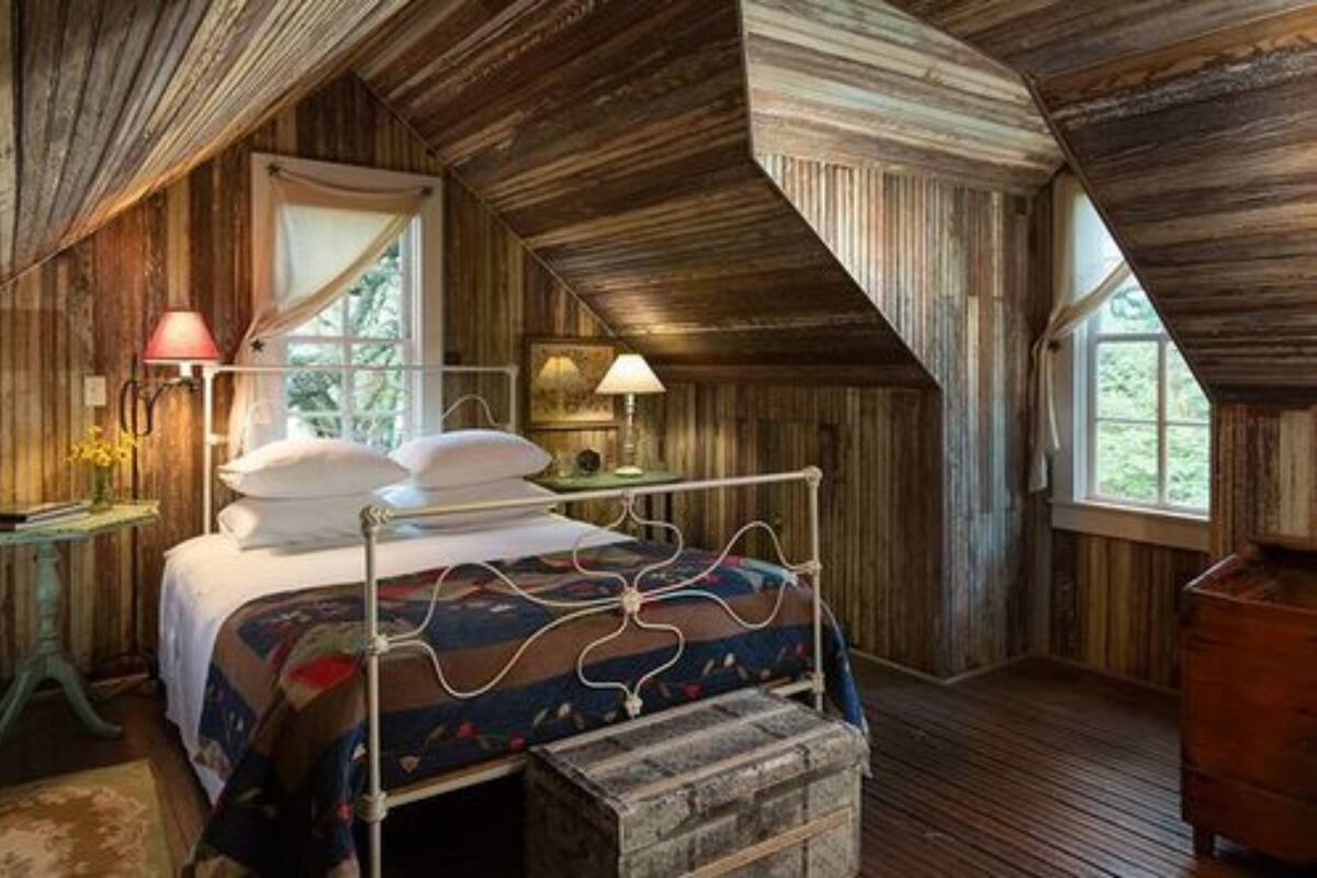Um quarto rústico de madeira com uma cama, duas luminárias de cabeceira e uma janela.