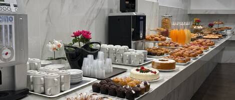 Buffet com diversos pastéis, uma máquina de café e um dispensador de bebidas.
