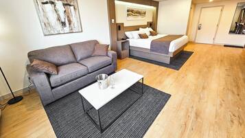 Quarto de hotel moderno com sofá cinzento, mesa de centro branca, cama com cabeceira cinzenta e obras de arte nas paredes.