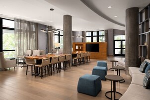 Um hall de hotel espaçoso com uma grande mesa de jantar de madeira, assentos confortáveis e uma tela de TV grande.