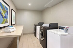 Uma lavanderia com máquina de lavar, secadora e uma mesa com toalhas dobradas.