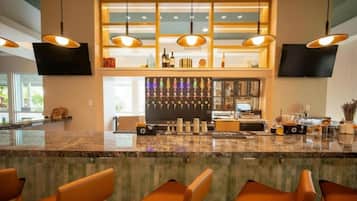 Uma área de bar com bancada de mármore, várias luminárias pendentes e uma televisão na parede.