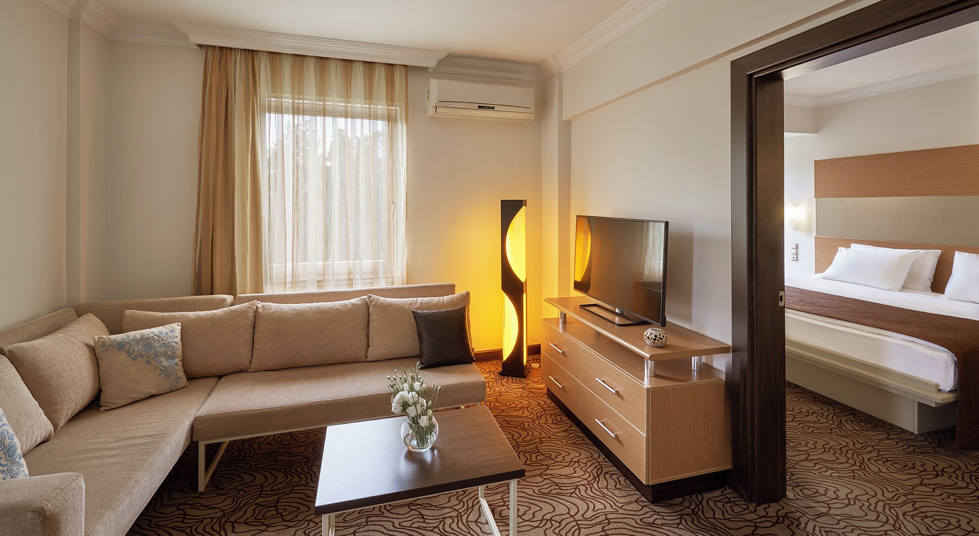 Quarto de hotel com sofá, televisão, mesa de cabeceira com um vaso e uma cama.