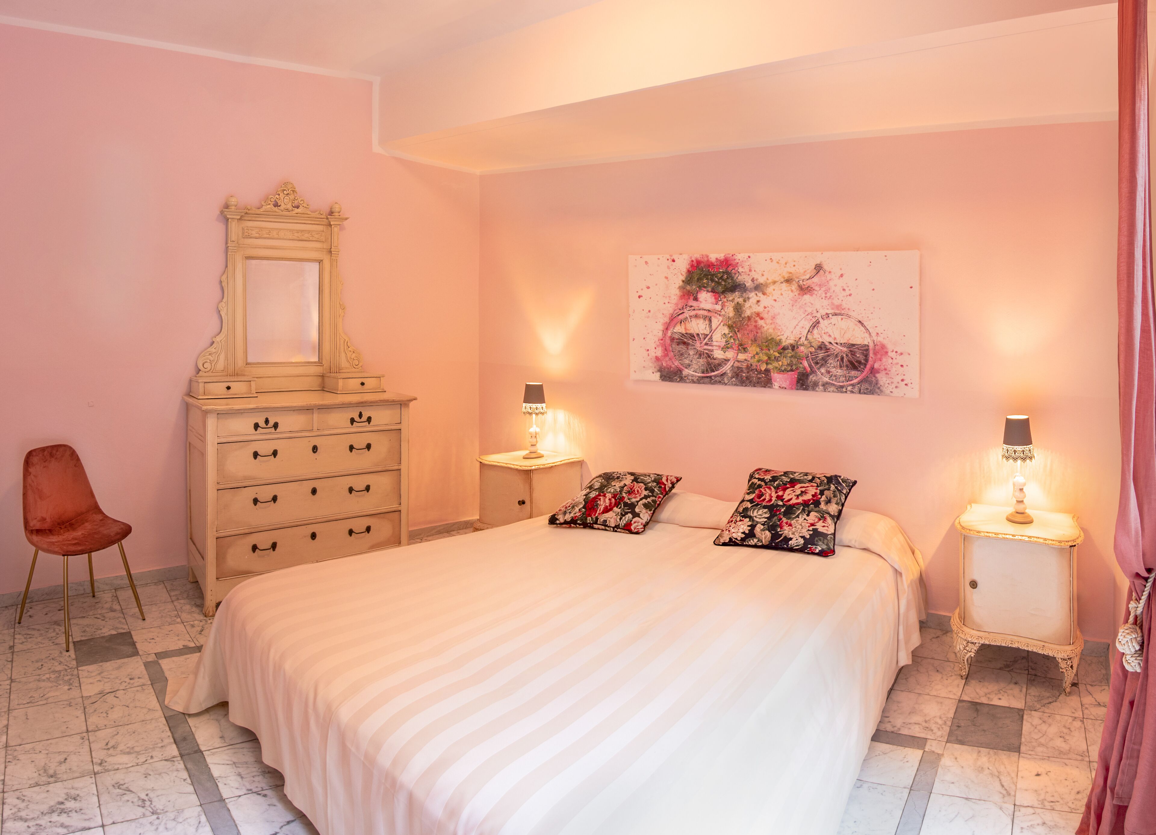 Quarto com cama, penteadeira, cadeira e duas mesas de cabeceira com luminárias.