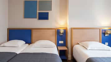 Quarto de hotel com duas camas, cada uma com cabeceira de madeira e uma pequena mesa de cabeceira com abajur.