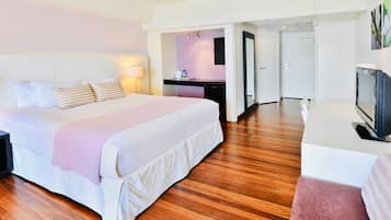 Quarto de hotel com uma cama grande, uma escrivaninha com computador e uma televisão.