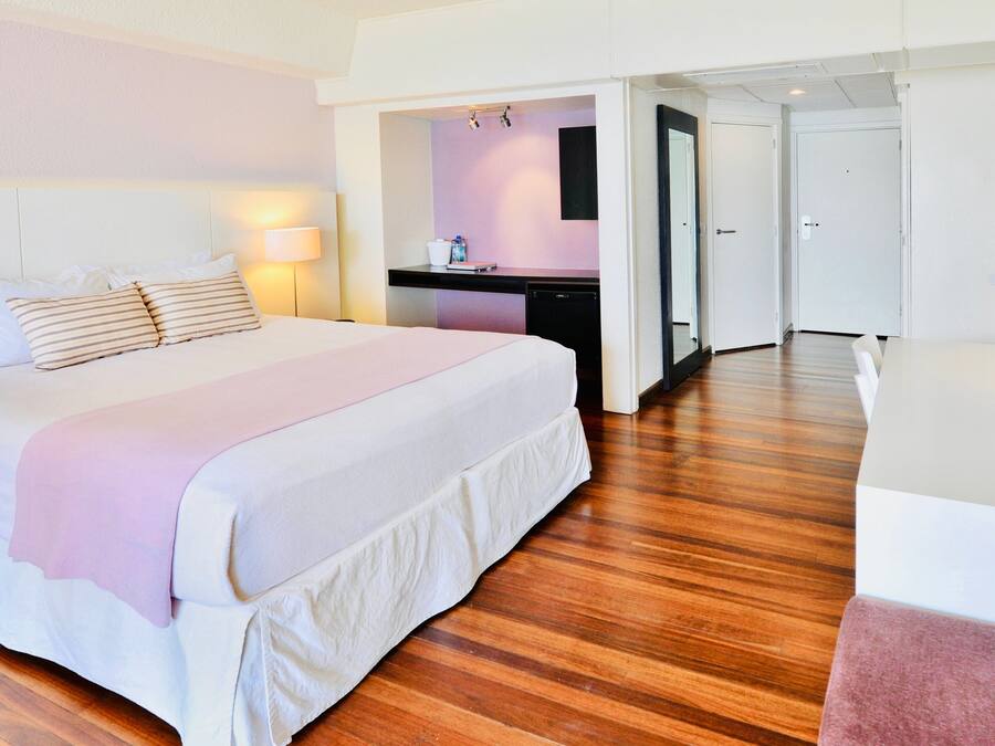 Quarto de hotel com uma cama grande, uma escrivaninha com computador e uma televisão.