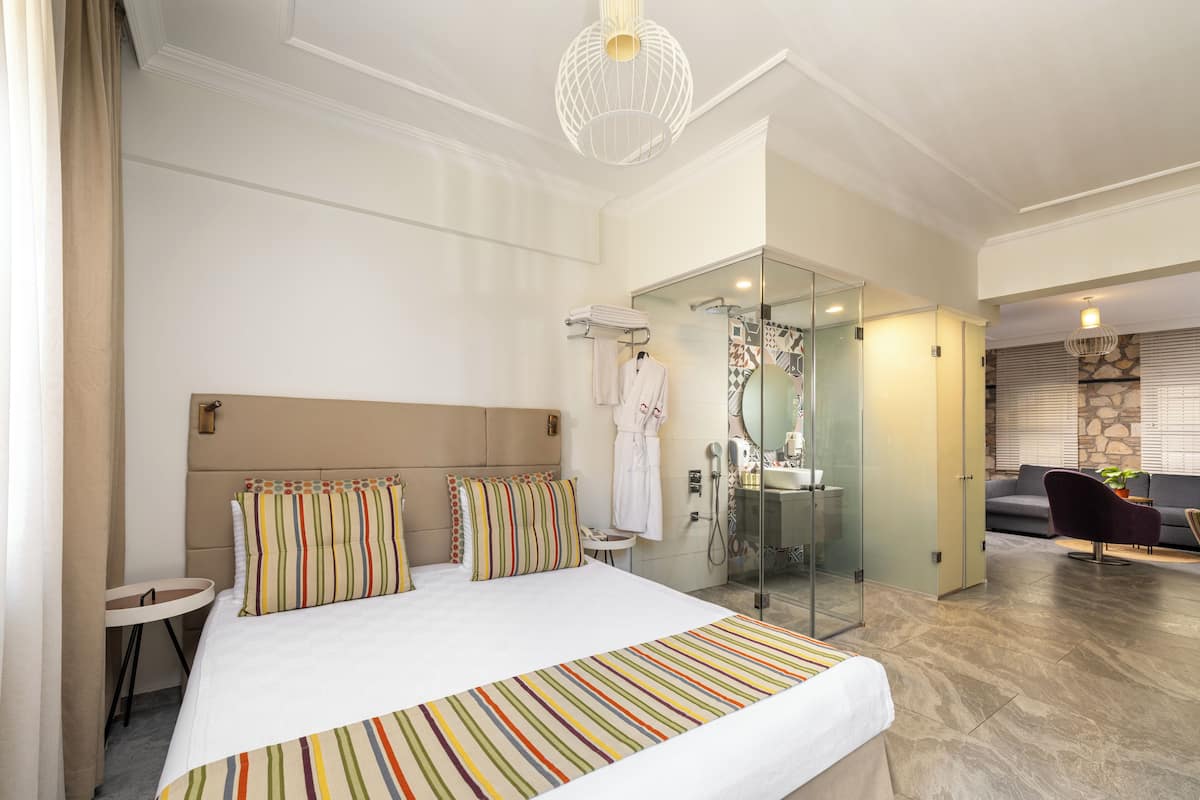 Quarto de hotel com cama grande, chuveiro em cabine de vidro, sofá e pequena mesa.