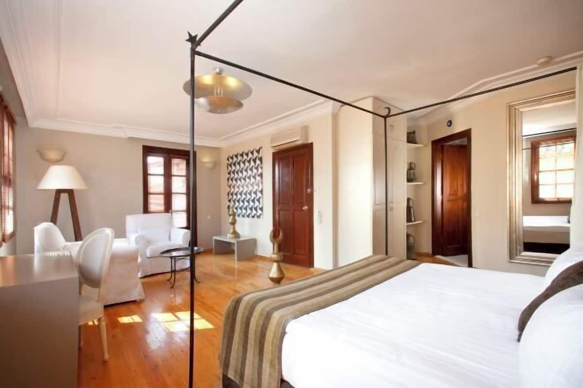 Quarto de hotel com cama, escrivaninha, cadeira, luminária, espelho e parede estampada.