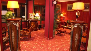 Um saguão de hotel com tapete vermelho, móveis de madeira e duas luminárias sobre pedestais.
