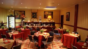 Espaço de refeições de hotel com várias mesas e cadeiras, um frigorífico e objetos decorativos.