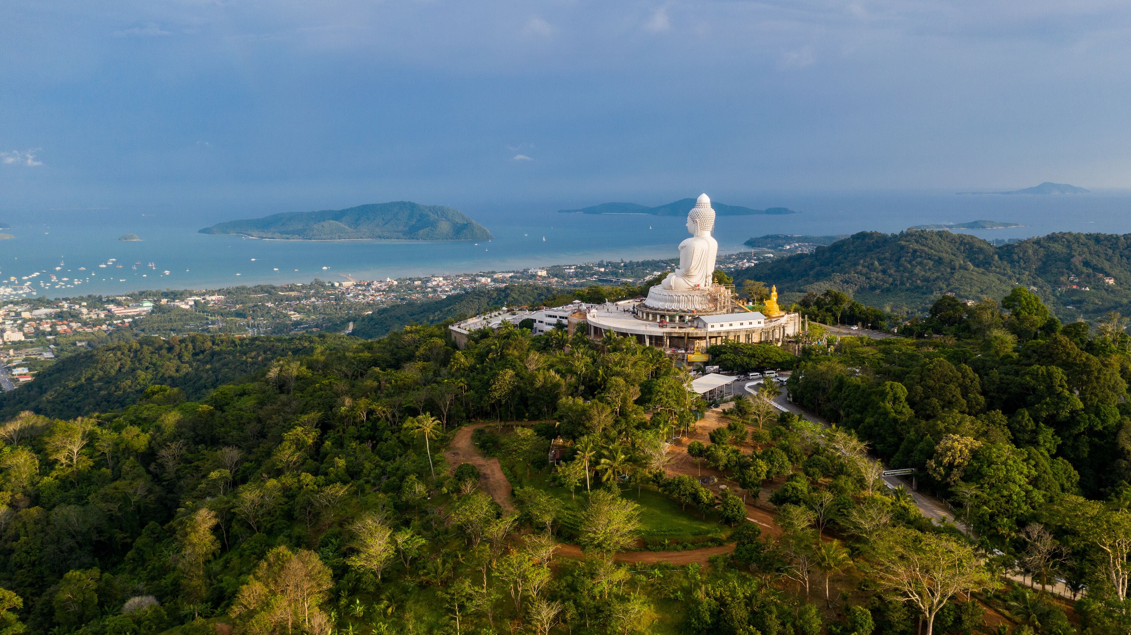 Uma grande estátua branca no topo de uma colina, com vista para uma cidade costeira e o mar.
