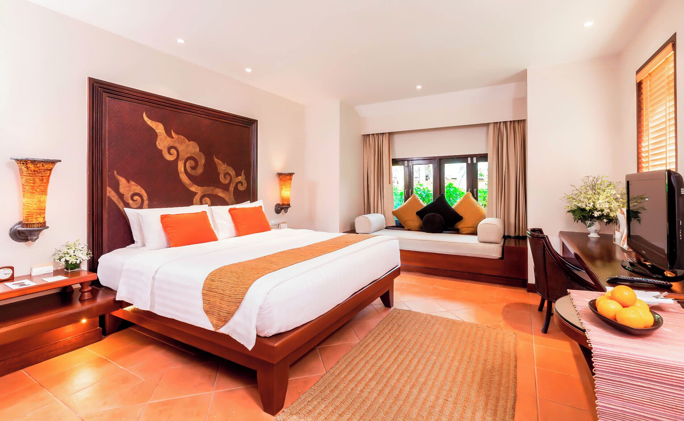 Quarto de hotel com cama grande, sofá, televisão e área de refeições com frutas.