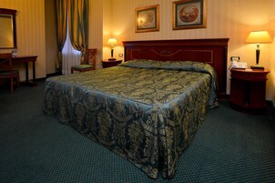 Quarto de hotel com uma cama grande, duas mesas de cabeceira, uma escrivaninha e uma cadeira.
