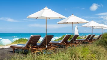 Na praia, areia branca, espreguiçadeiras, toalhas de praia