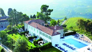 Uma casa grande com piscina, rodeada por vegetação exuberante e vinhedos.