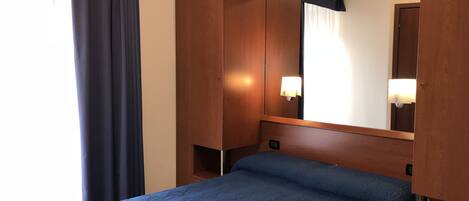 Quarto de hotel com cama, guarda-roupa de madeira, espelho e mesa de cabeceira.