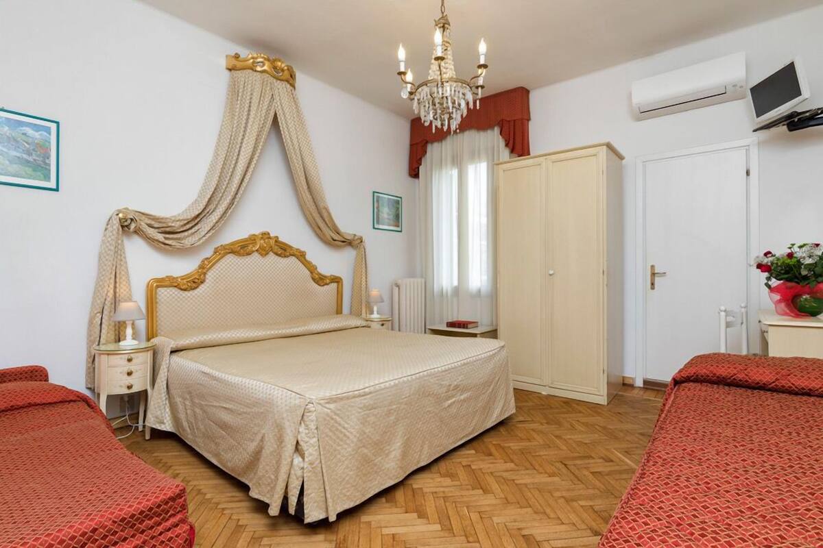 Quarto com cama grande, lustre, guarda-roupa e mesa de cabeceira com abajur.