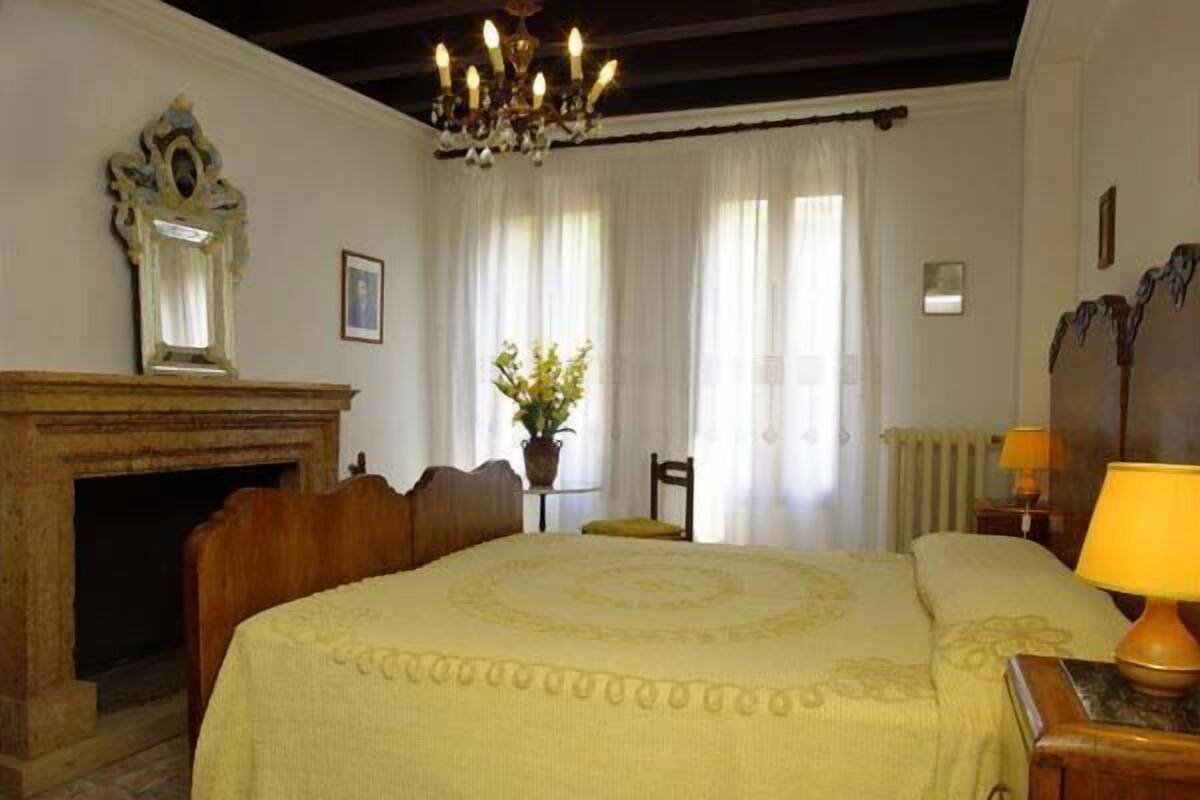 Quarto tradicional com uma cama grande, lareira, lustre e janela com cortinas.