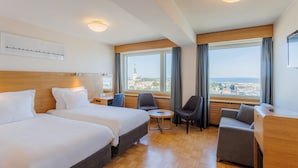 Quarto de hotel com duas camas, uma escrivaninha, uma cadeira e vista para a cidade.