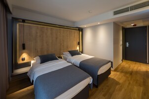 Quarto de hotel moderno com duas camas, cabeceira de madeira e porta escura.