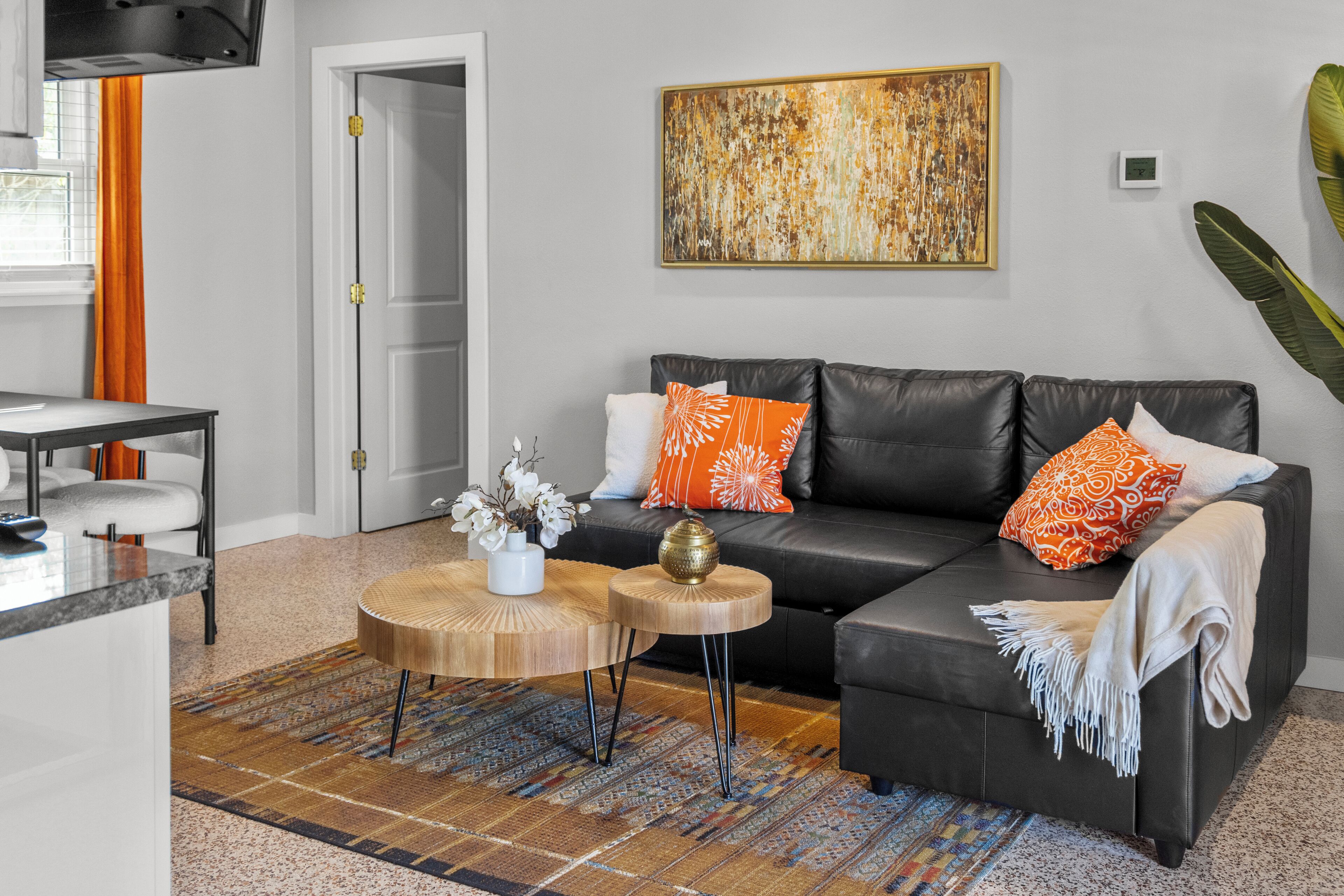 Uma sala de estar moderna com um sofá de couro preto, uma mesa de centro redonda de madeira e um tapete estampado.