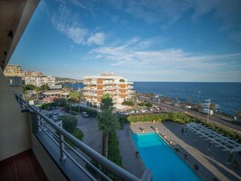 Uma varanda com vista para uma piscina, uma estrada e um edifício com vários andares.