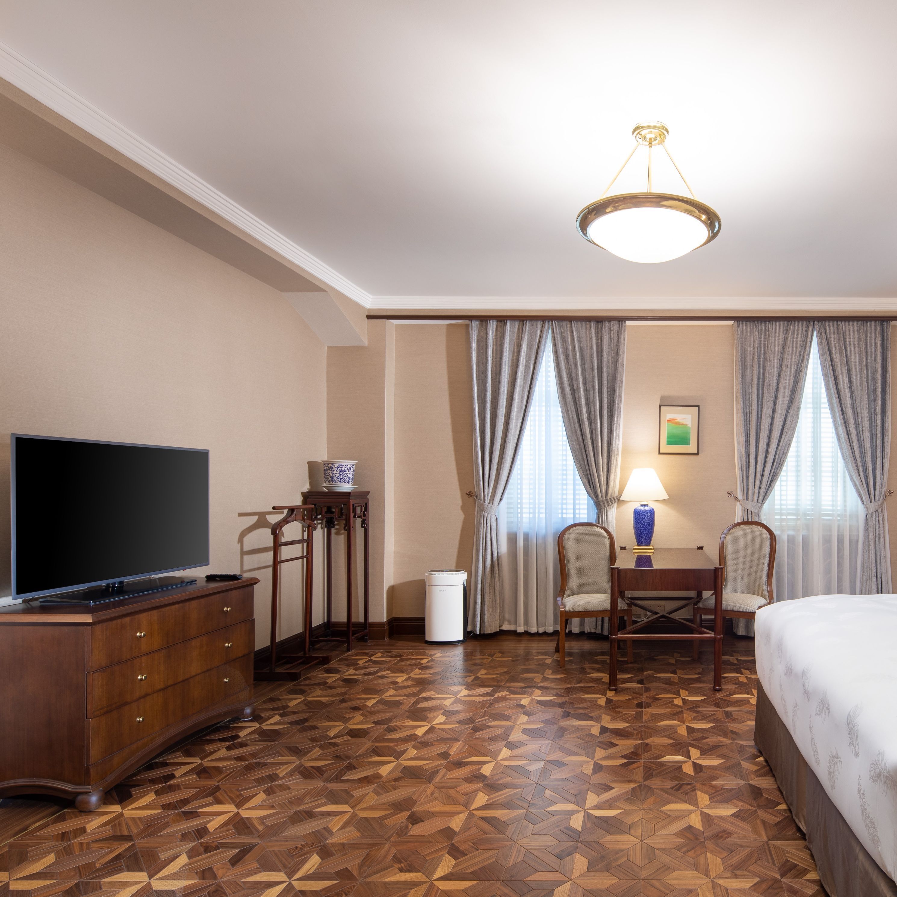 Quarto de hotel com televisão de tela plana, mobiliário de madeira, piso estampado e uma cama.