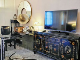 Uma sala de estar moderna com uma grande televisão de tela plana, uma mesa de centro de vidro, um rádio antigo e um abajur decorativo.