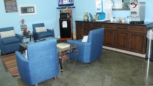 Uma sala de estar com sofás azuis, uma máquina de café, uma televisão e um relógio na parede.