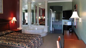 Quarto de hotel com cama grande, área de estar, banheiro e cozinha compacta.