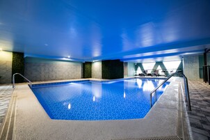 Piscina interior com água azul cristalina, rodeada por paredes revestidas de azulejos e teto pintado de azul.