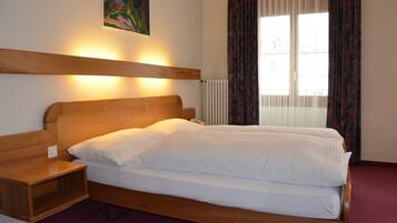 Cama bem arrumada com lençóis brancos em quarto com cabeceira e mesa de cabeceira de madeira.