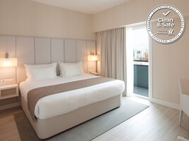 Quarto de hotel limpo e seguro com uma cama, mesas de cabeceira e vista para a cidade pela janela.