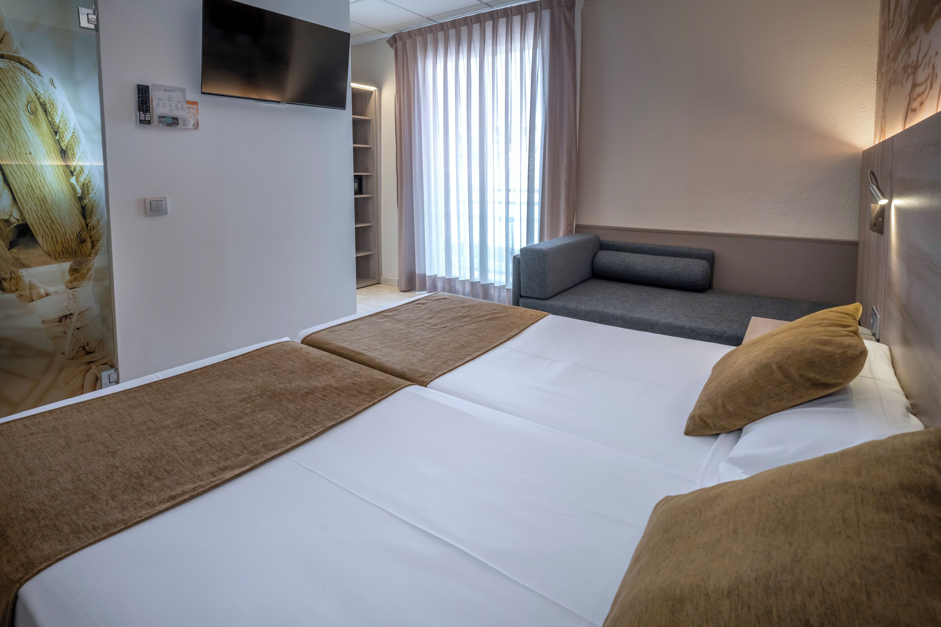 Quarto de hotel com cama, sofá, televisão e janela com cortinas.
