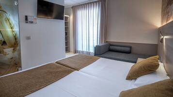 Quarto de hotel com cama, sofá, televisão e janela com cortinas.