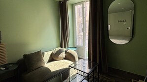Quarto com sofá, mesa de centro de vidro, espelho e vista para prédios pela janela.