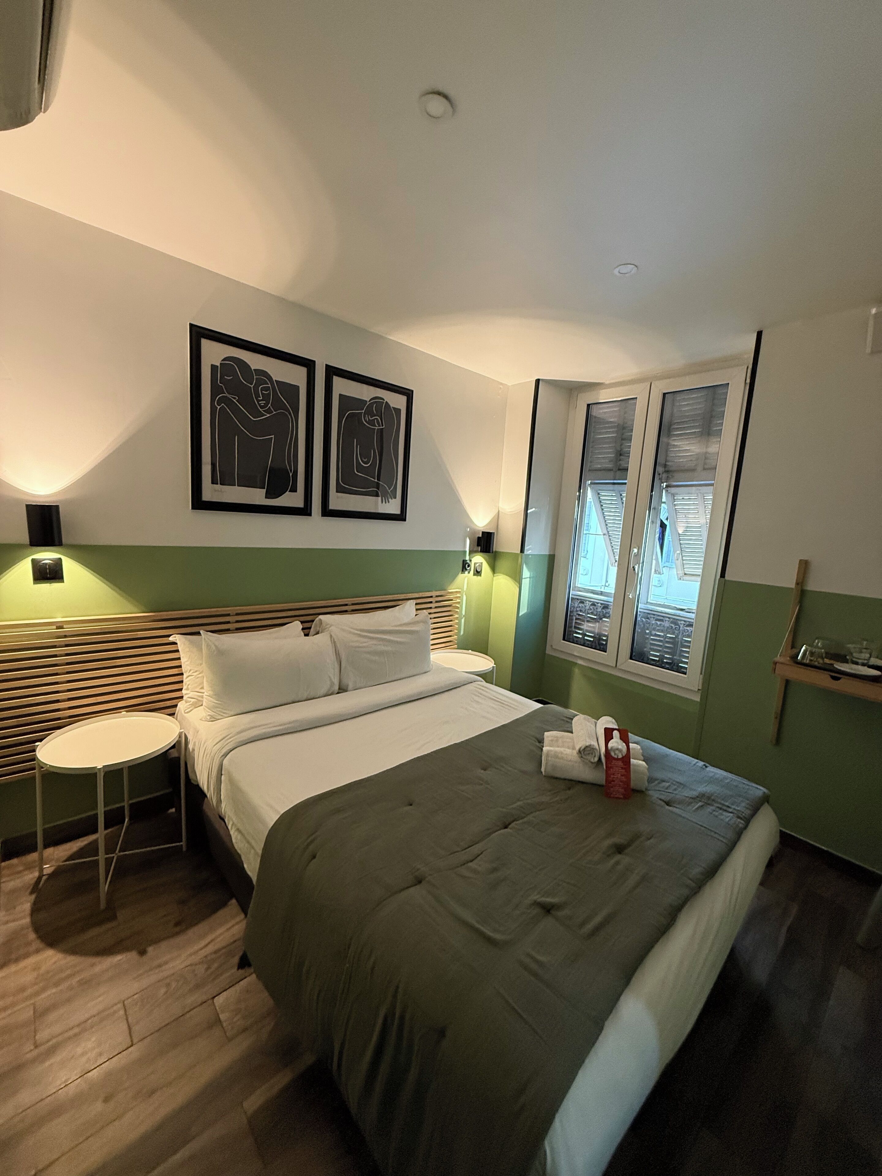 Quarto de hotel com cama, mesa de cabeceira e duas obras de arte emolduradas na parede.