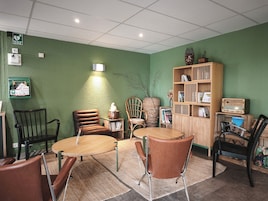 Um quarto acolhedor com parede verde, uma estante de madeira, uma mesa redonda e cadeiras de couro.