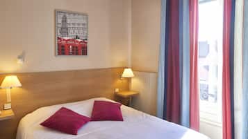 Quarto de hotel com cama, duas luminárias de cabeceira, um quadro na parede e uma janela com cortinas.