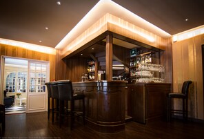 Uma área de bar com balcões de madeira, bancos e prateleiras cheias de garrafas e copos.