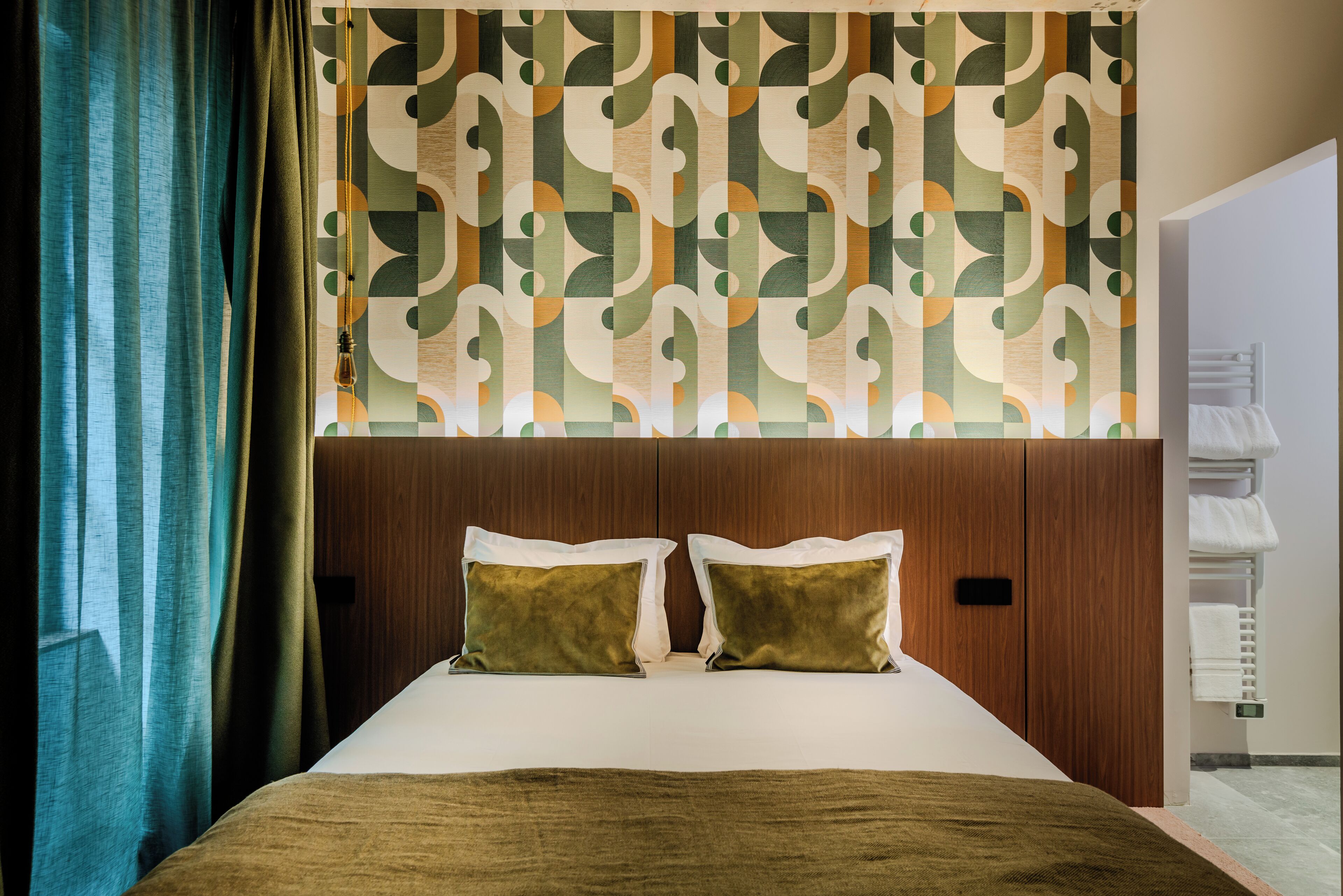 Quarto de hotel com cabeceira de madeira, parede estampada e uma cama com dois travesseiros.