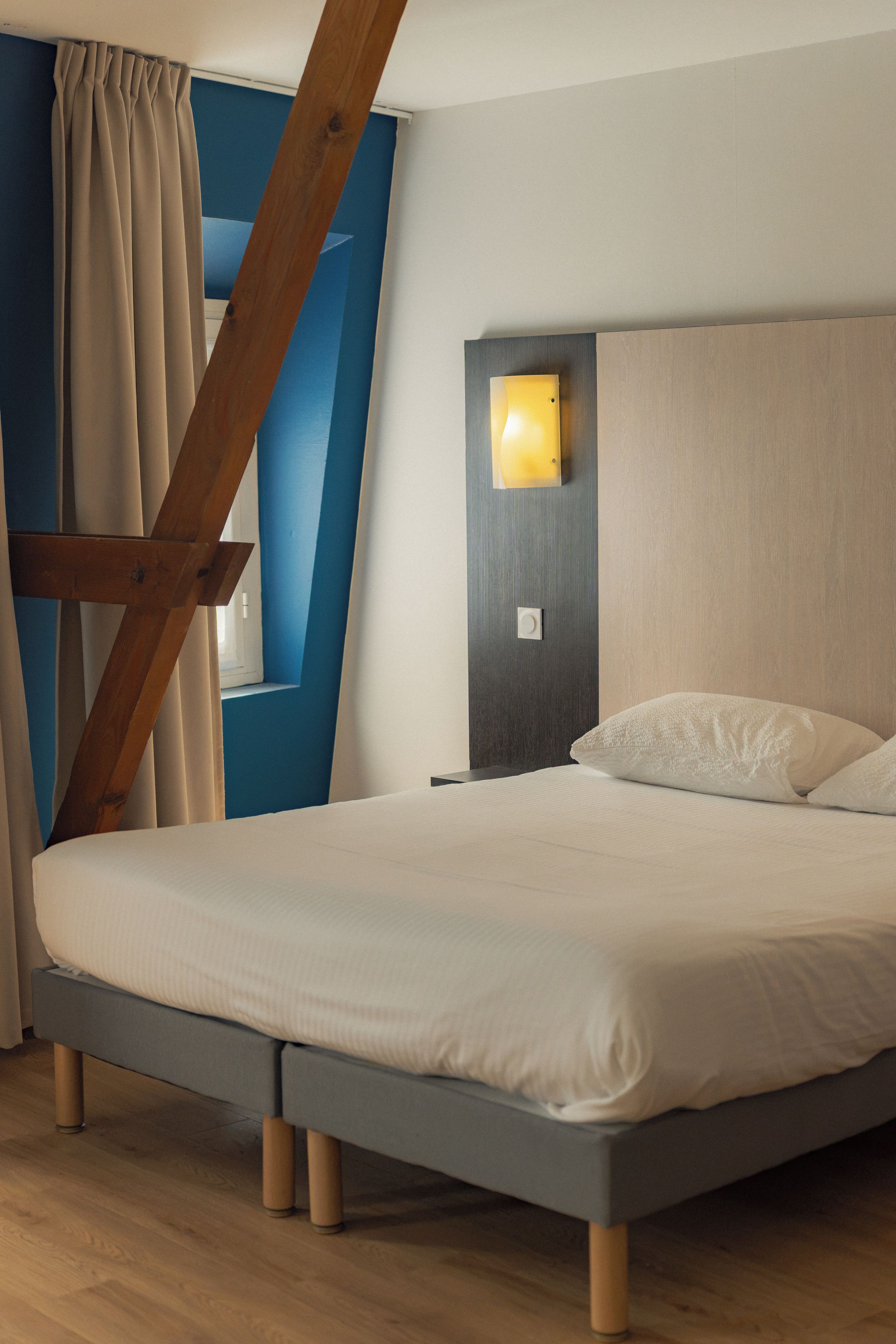 Quarto moderno com cama, mesa de cabeceira, luminária na parede e janela com cortinas.