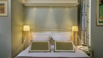Cama bem arrumada com duas almofadas, duas luminárias de cabeceira e uma mesinha de cabeceira com um livro e óculos.
