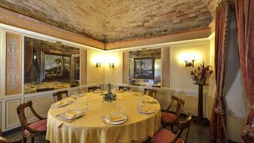 Uma sala de jantar com teto de tijolos, decoração de parede elaborada e uma mesa redonda posta para seis pessoas.