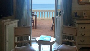 Quarto com vista para o mar, televisão, escrivaninha e duas cadeiras.
