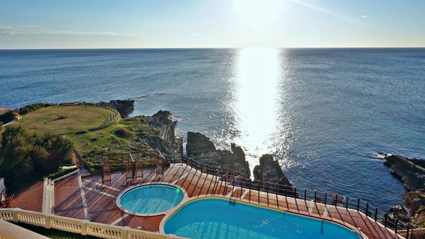 Um resort com piscina, vista para o oceano e terreno rochoso.