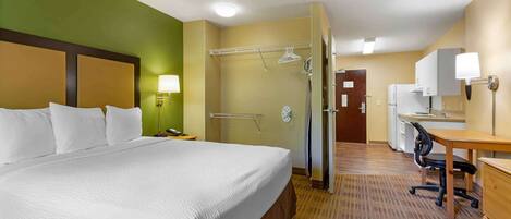 Quarto de hotel com uma cama grande, uma escrivaninha, uma cadeira, chuveiro e uma cozinha compacta.