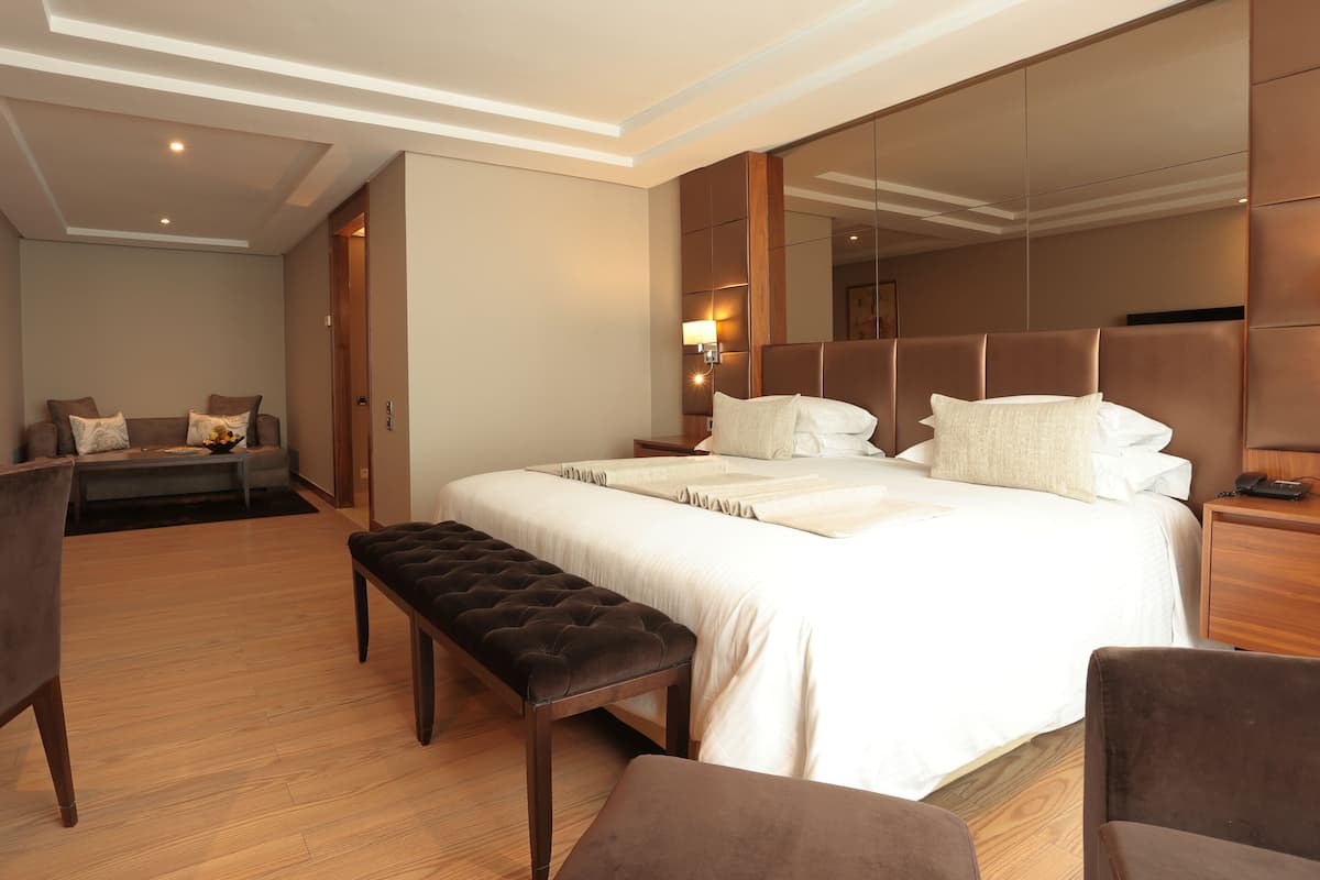 Quarto de hotel com uma cama grande, um sofá, um banco e piso de madeira.