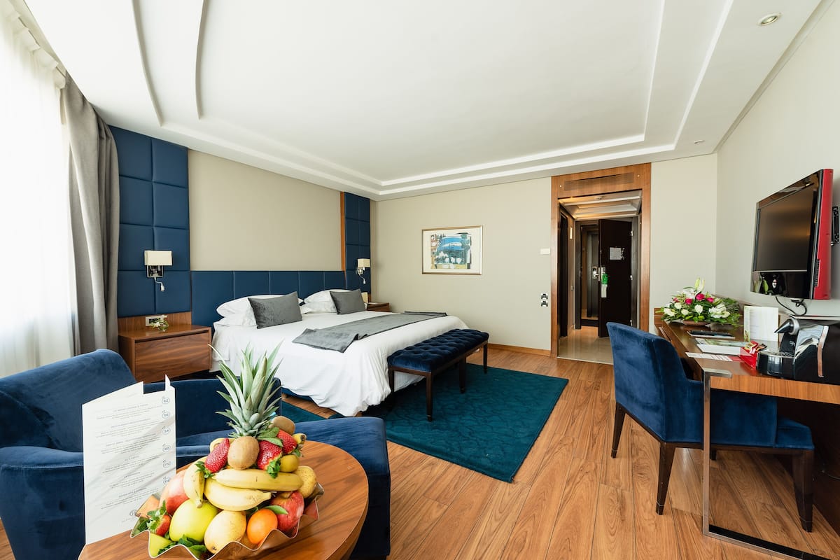 Quarto de hotel com cama, escrivaninha, cadeira, mesa de jantar e uma televisão.